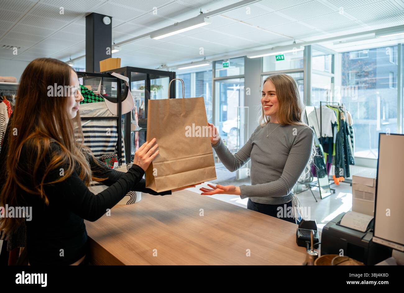 Female shop assistant giving paper bag to customer in clothing store ...