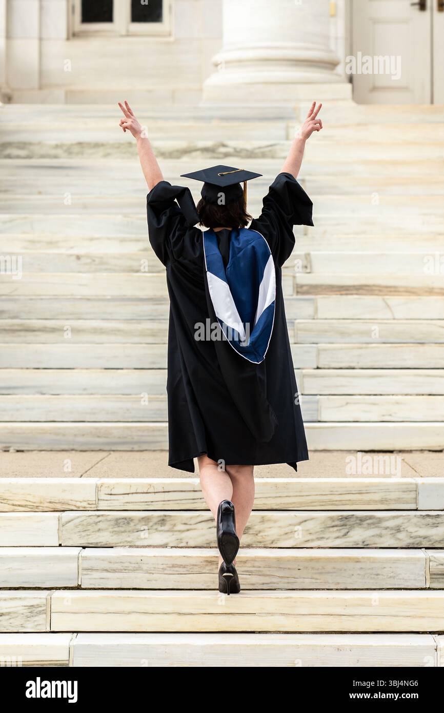 back of young female in a graduation cap and gown on marble stairs ...