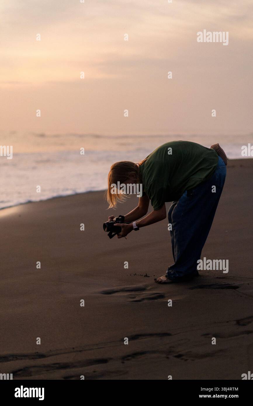 Photographer crouching on the sand to capture a low-angle beach shot ...