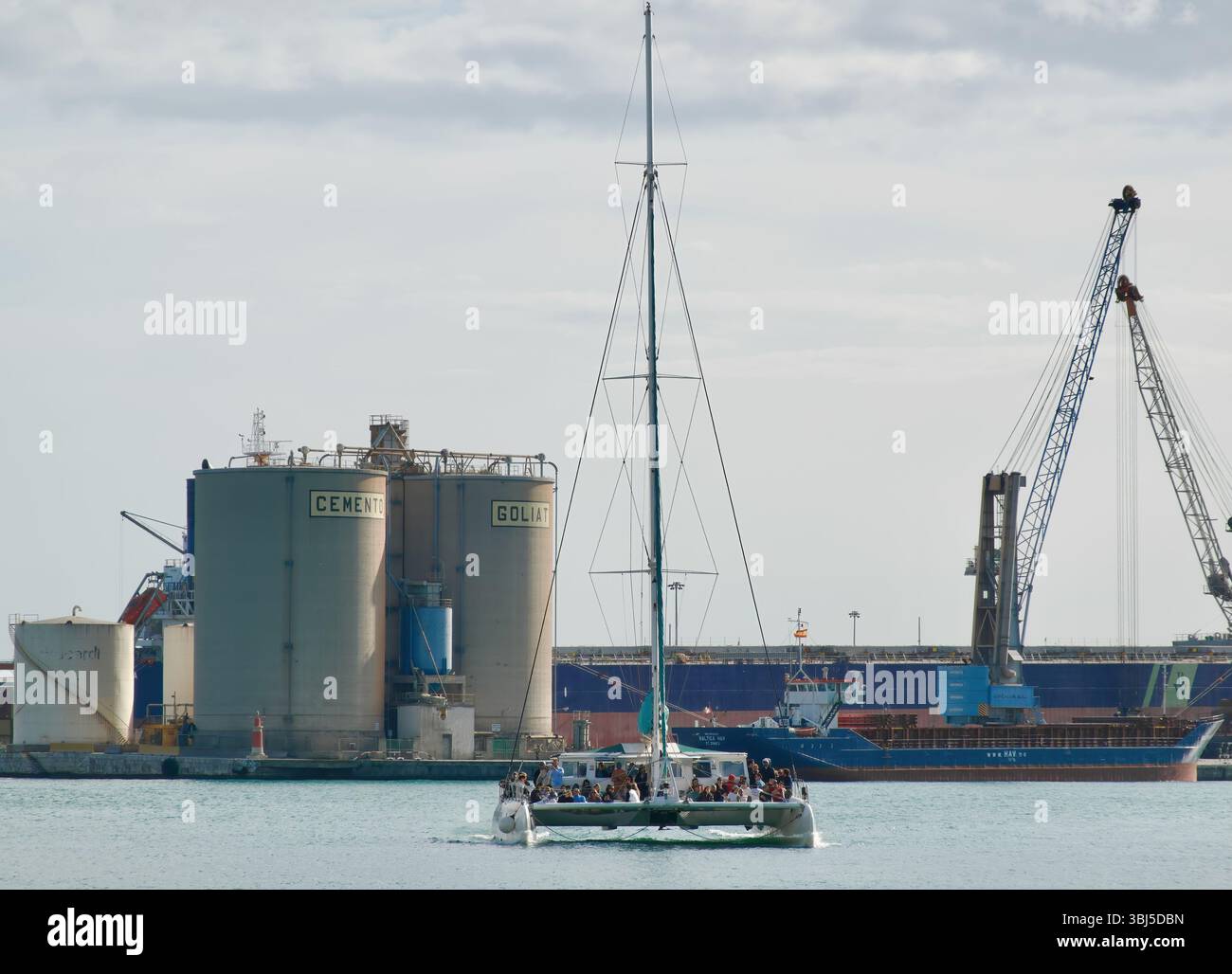 Port of Malaga with a tourist catamaran returning with cement storage ...