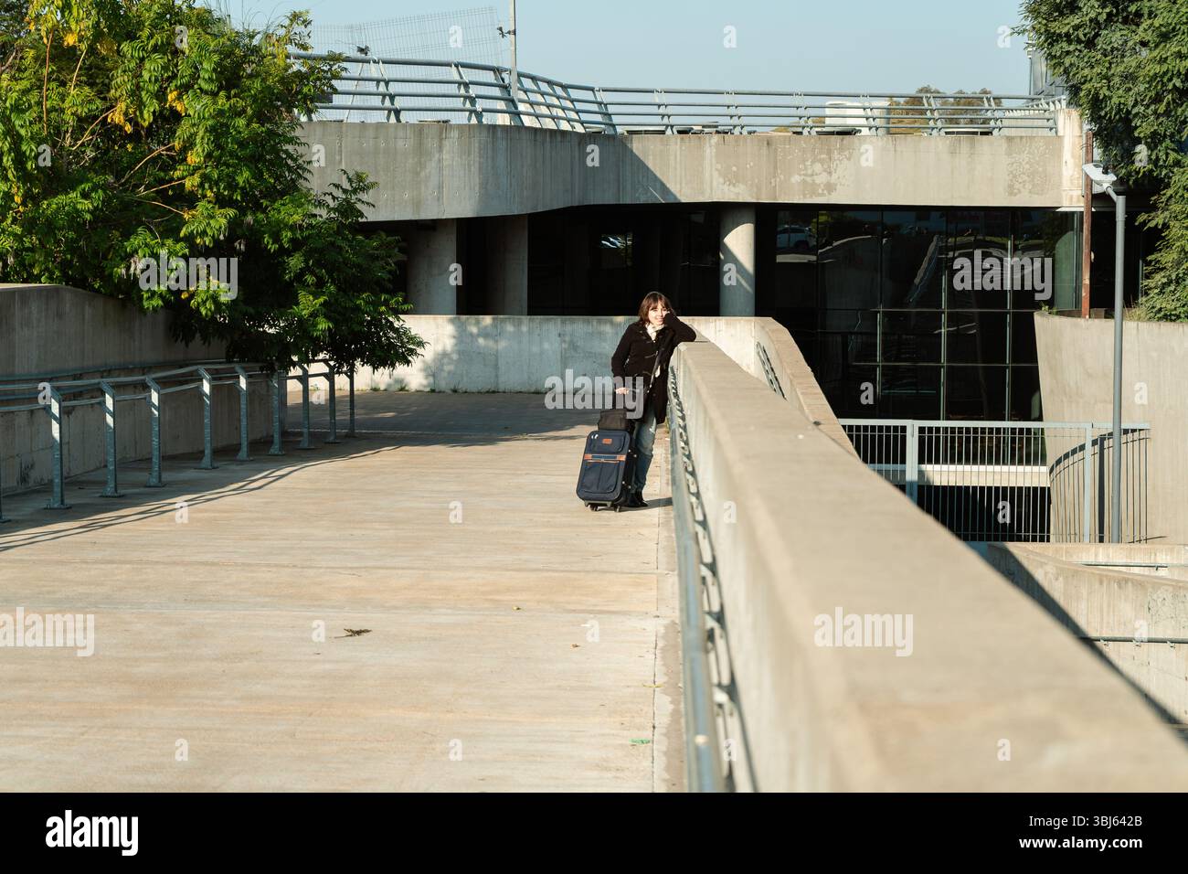 Young woman pulling wheeled luggage while walking up a wide concrete ...