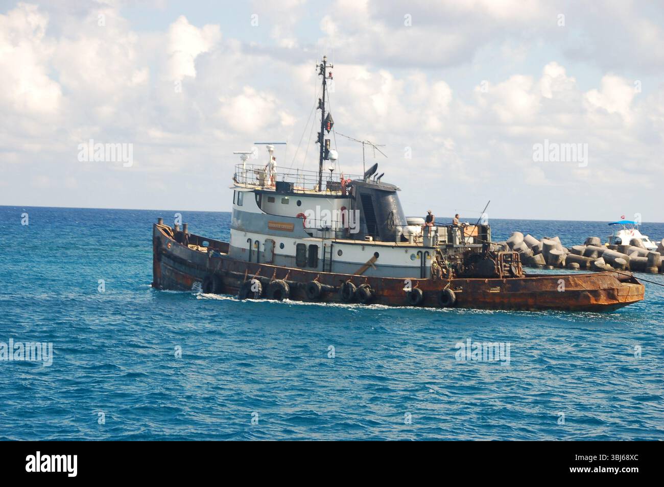 Rusty tugboat sails near a breakwater on a sunny day in clear blue ...