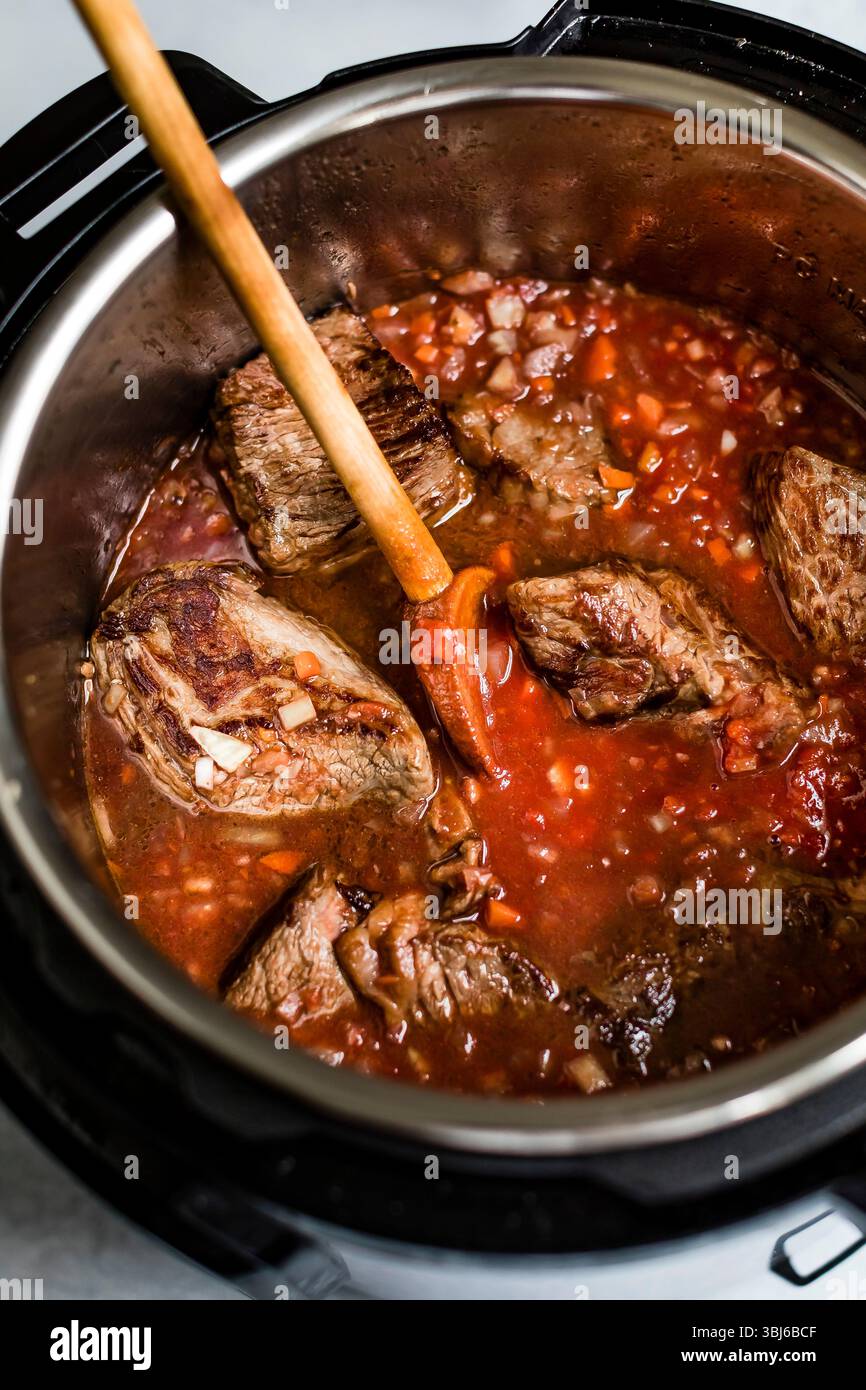Chunks of beef cooking in a tomato-based sauce inside an electric ...