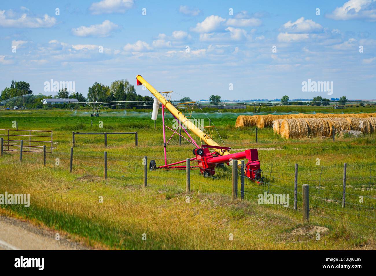 Grain auger and hay bales on a summer farm field in Alberta, Canada ...