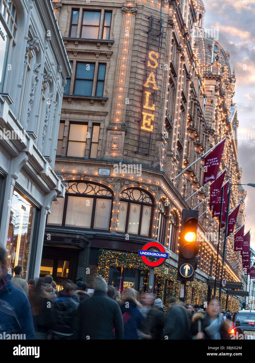 Harrods department store at dusk sunset with lit 'Sale' sign and crowds ...