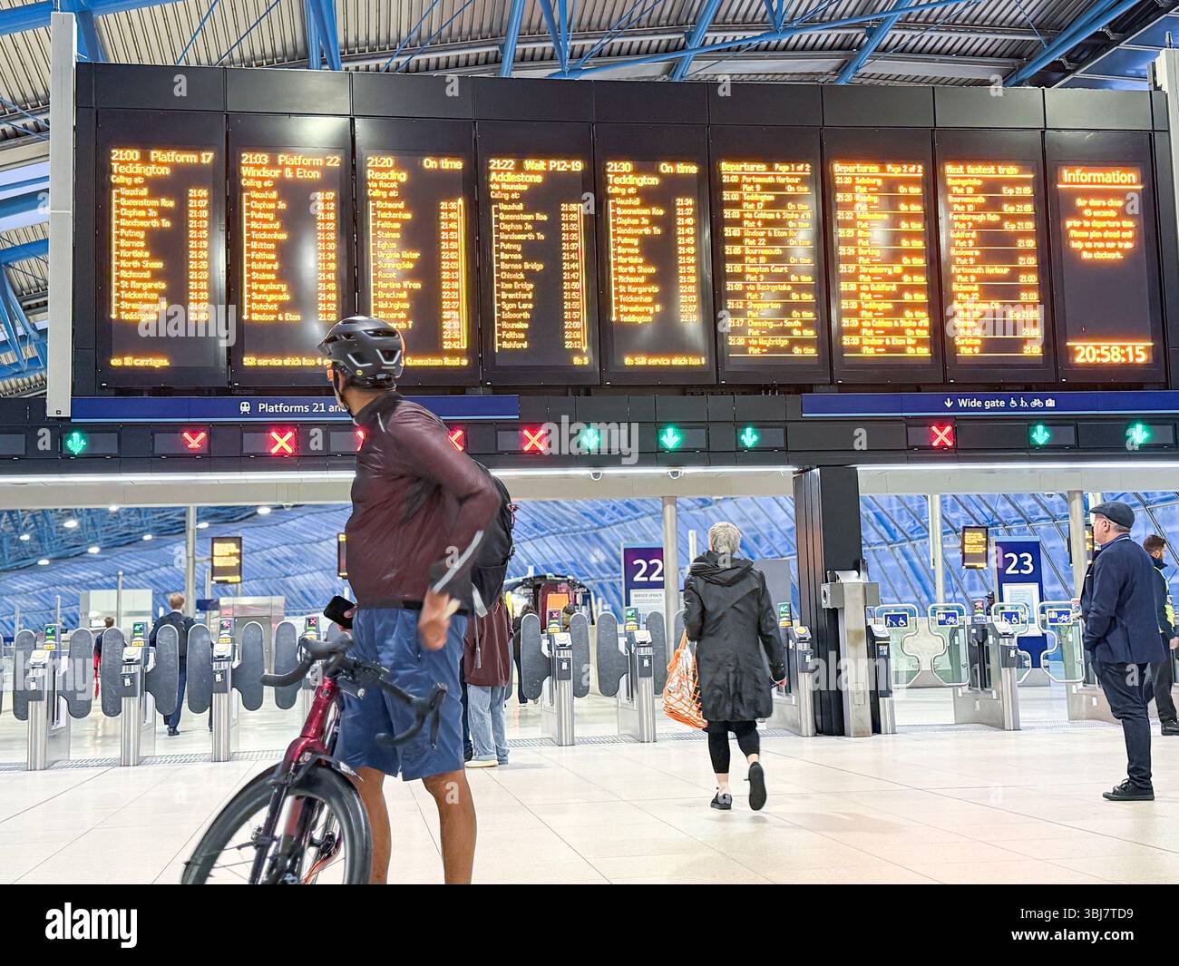 cyclist and Commuters check train info on digital LED screen above ...