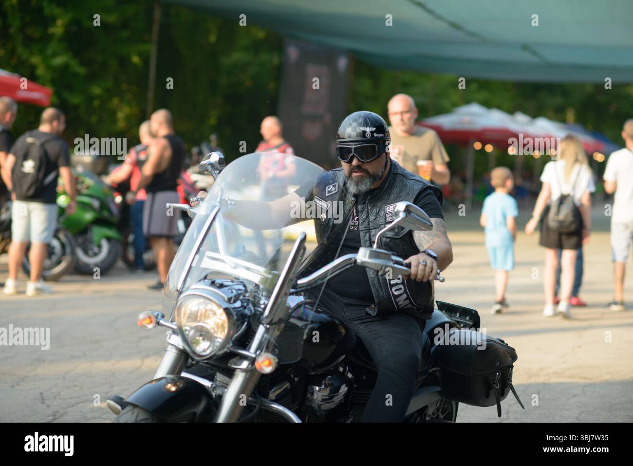 A biker wearing a black leather vest, helmet, and riding goggles ...