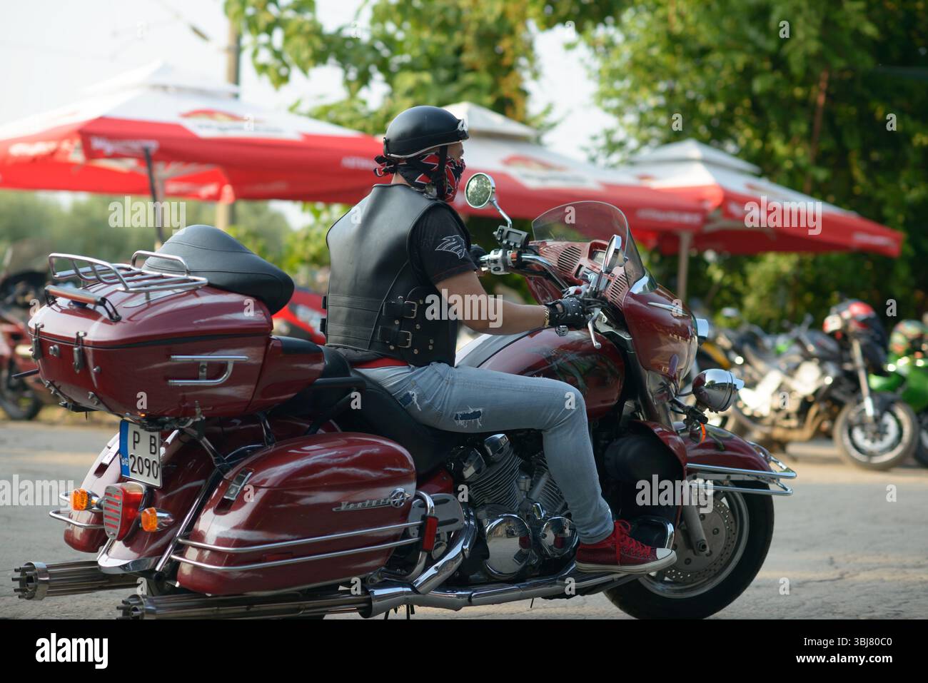 A biker wearing a helmet, leather vest, gloves, and a red face covering ...