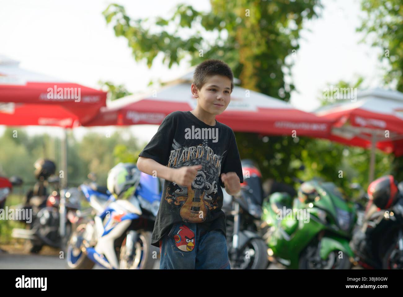 A young boy wearing a Hard Rock Cafe t-shirt walks near a row of parked ...