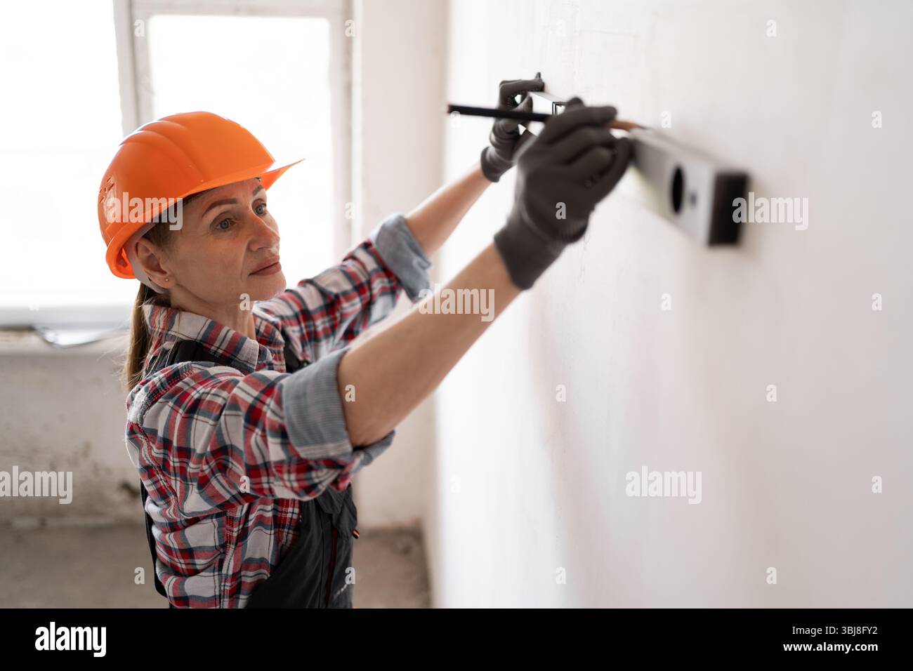 Builder checking wall using spirit level making marks with pencil ...