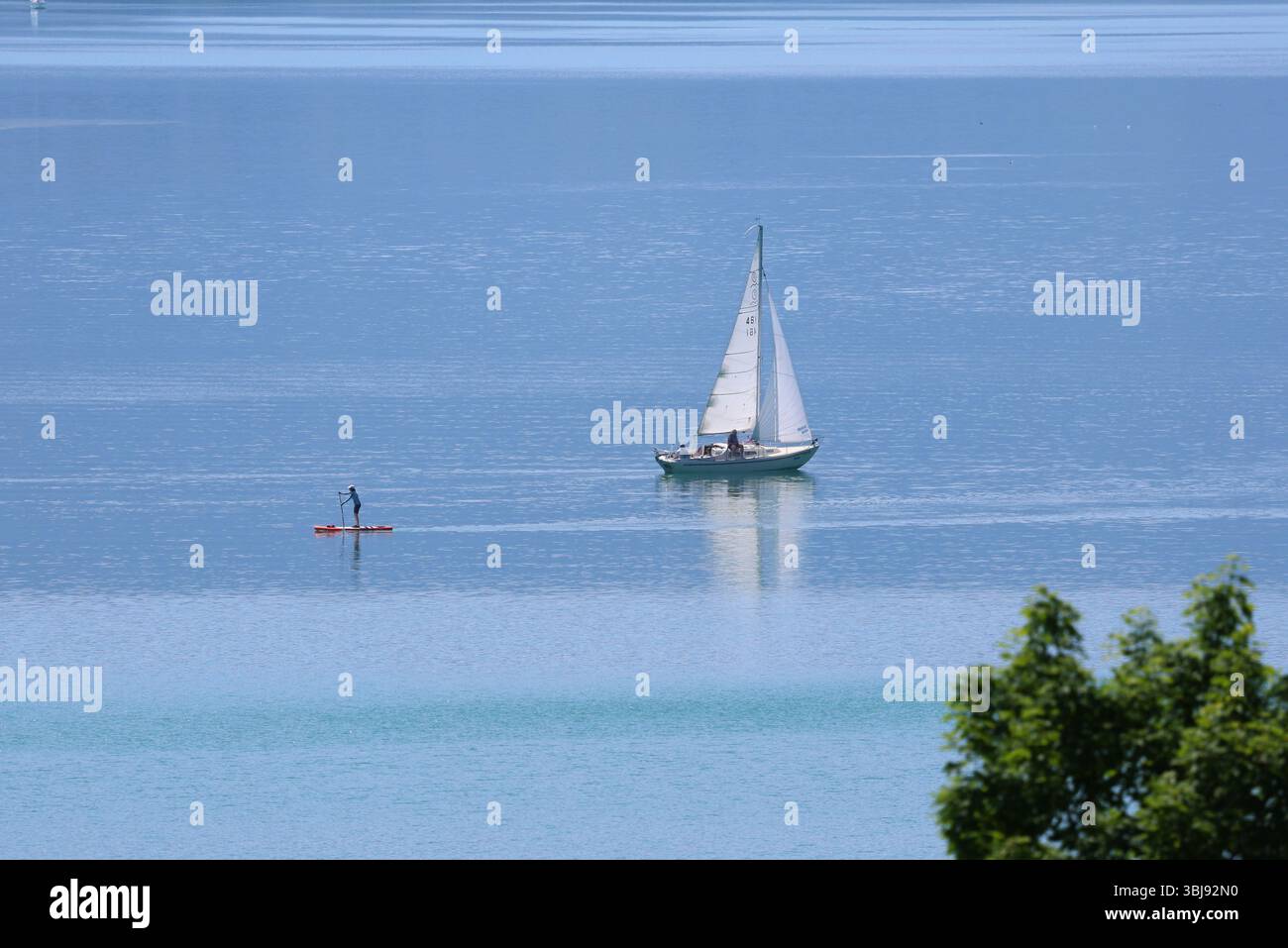 14 June 2025, Bavaria, Roßhaupten: A stand-up paddler (l) and a sailing ...