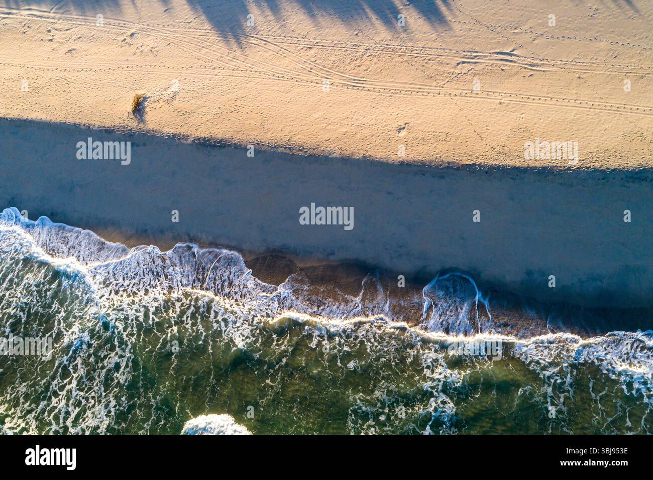 aerial view of ocean waves breaking on a wide sandy beach at sunset ...