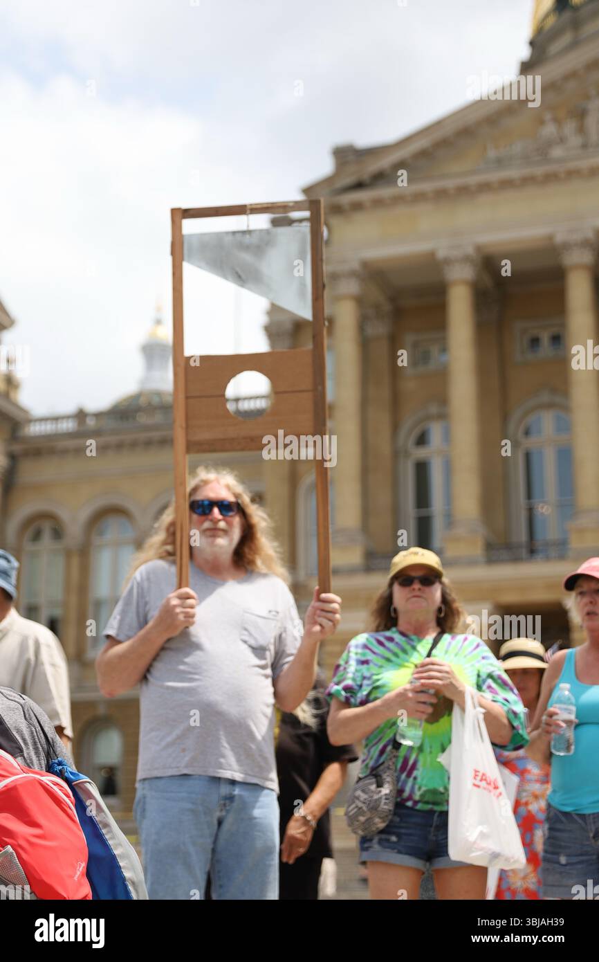 Des Moines, Iowa, USA. 14th June, 2025. A man holds a model guillotine ...
