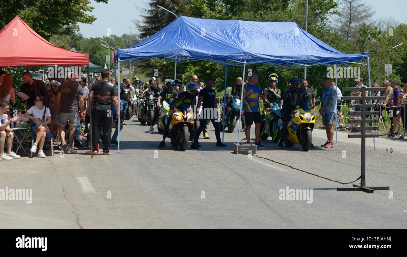 Motorcyclists line up under a blue canopy at the startline of a drag ...