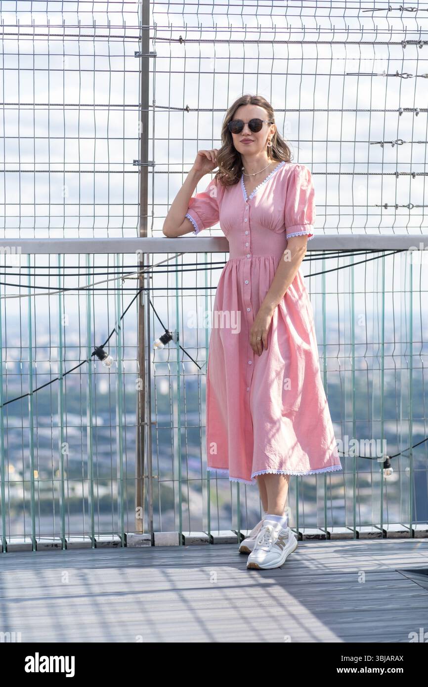 A woman poses elegantly in a pink dress and sunglasses while enjoying ...
