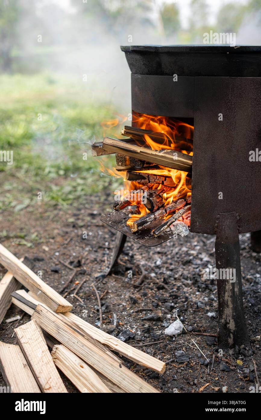 A cooking pot sits on a stove above an open flame while firewood is ...