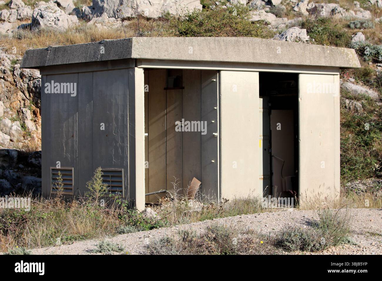 Small concrete utility shed with a flat roof and open metal door stands ...