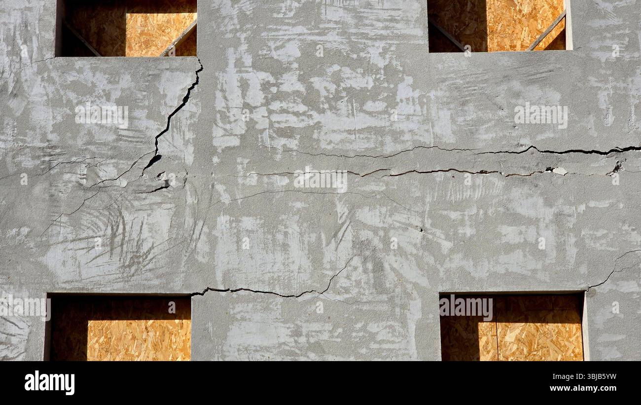 Close-up of gray concrete wall with deep horizontal and vertical cracks ...