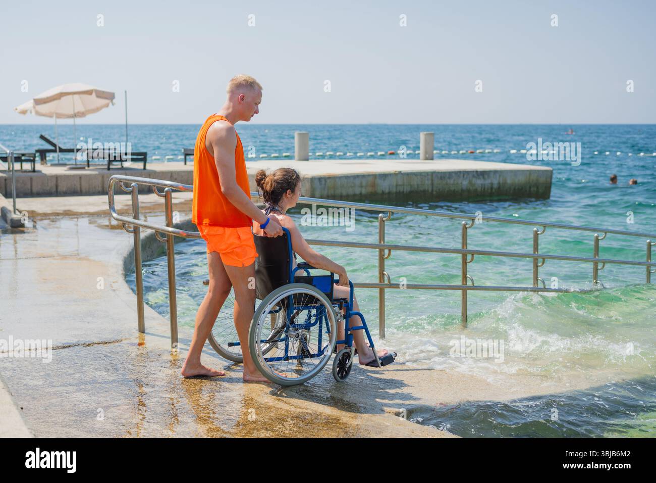 Lifeguard helping a woman with disability enter the water across the ...