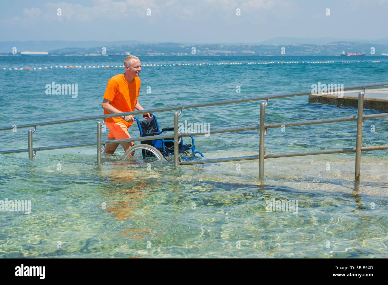 Smiling lifeguard rolling an empty aquatic wheelchair along an ...