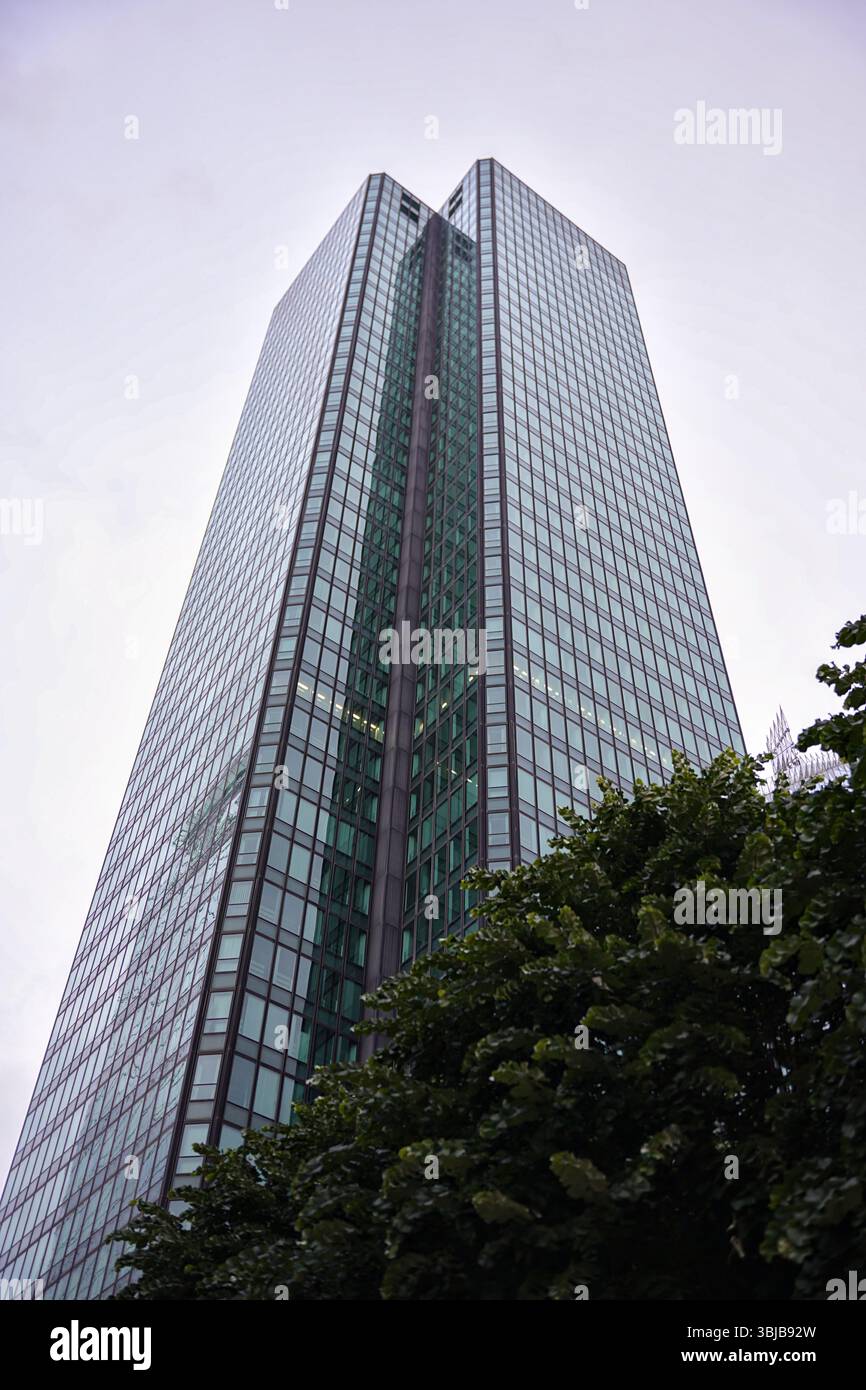 Tall modern glass tower in La Defense Paris rises above green trees ...