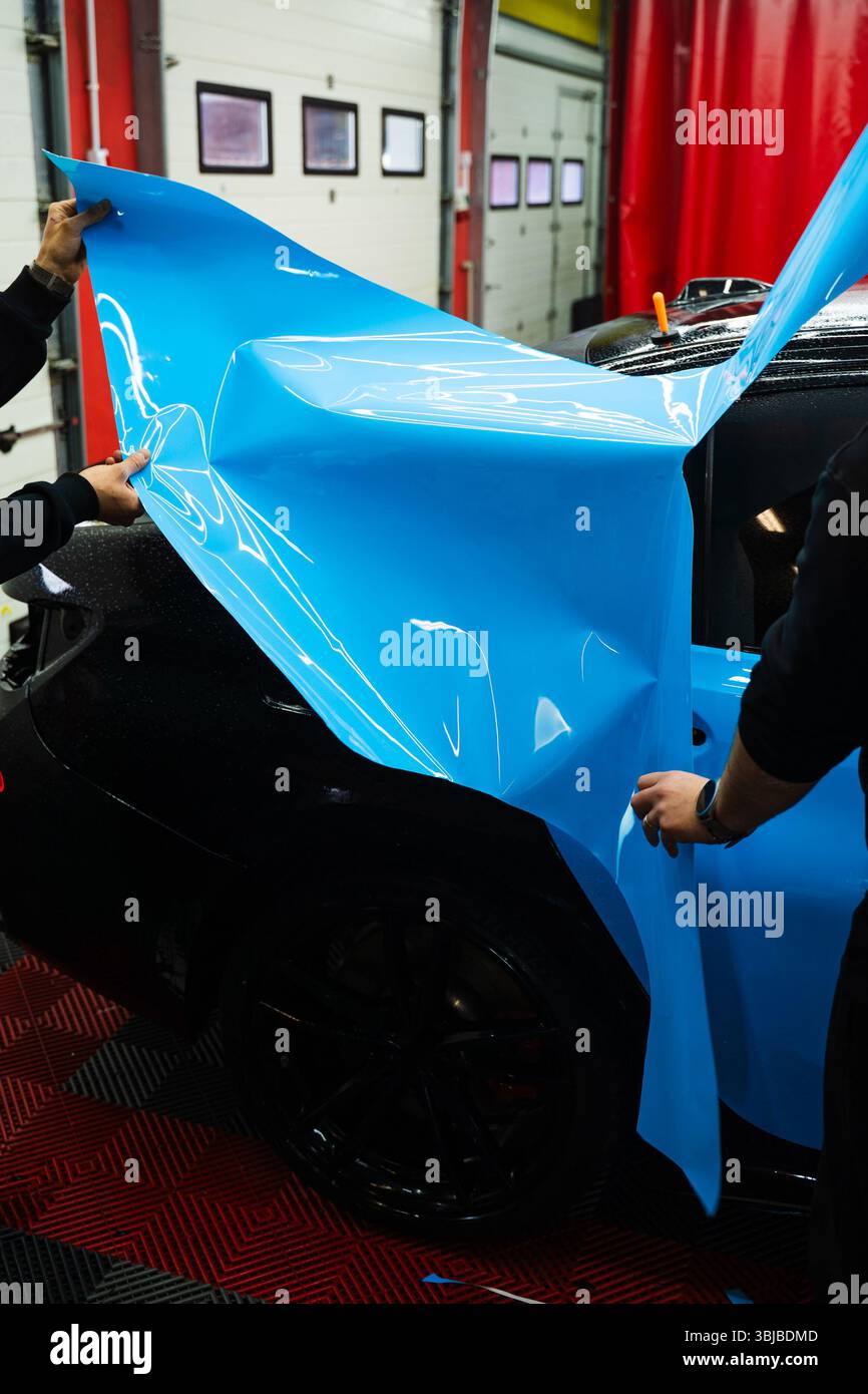 Applying PPF wrap on car during full detailing. Bold blue vinyl wrap ...
