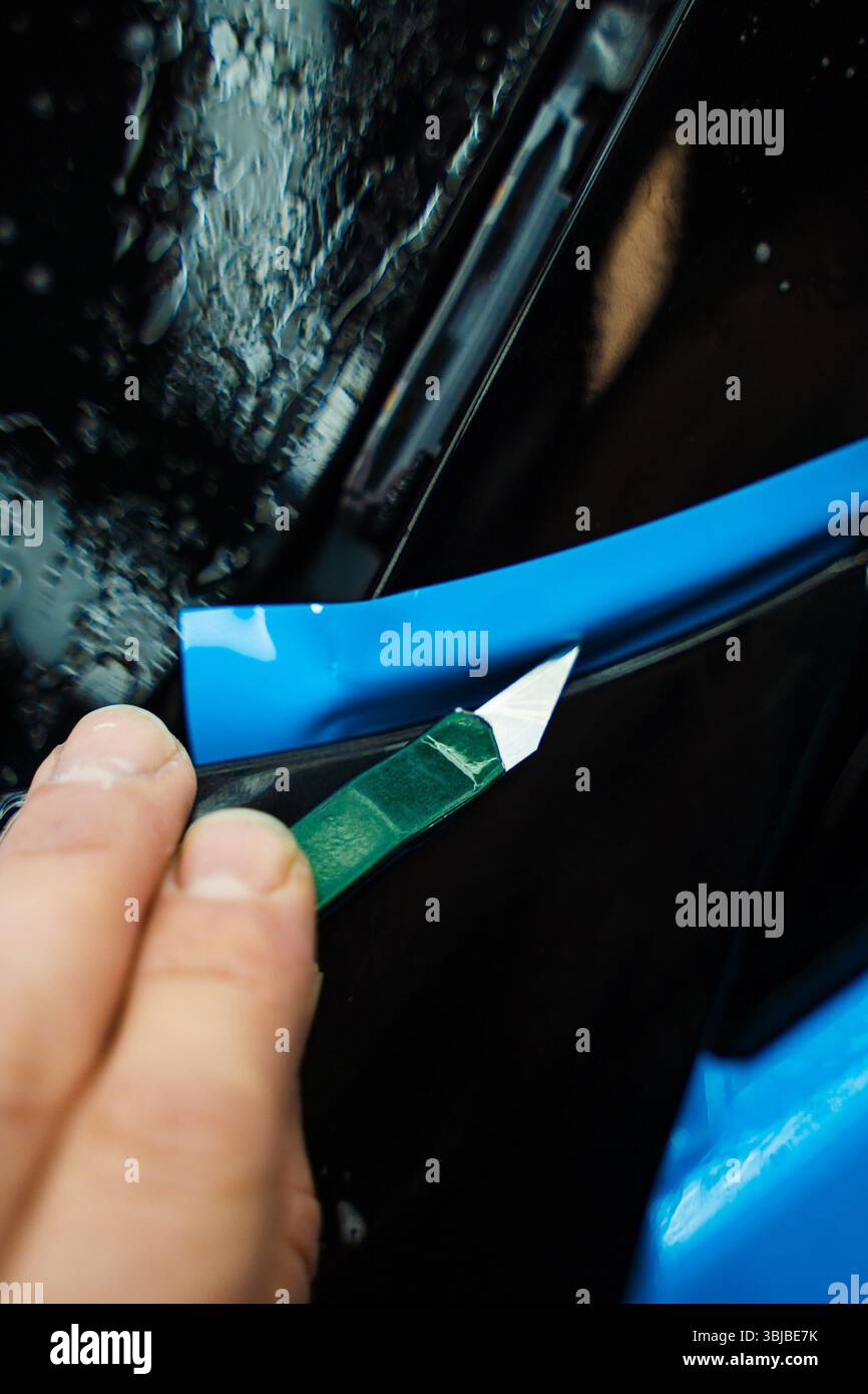 Detailing technician trims blue PPF on a car panel for perfect contour ...
