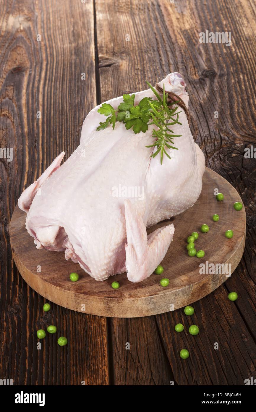 Raw whole chicken with fresh herbs and peas on brown wooden textured ...