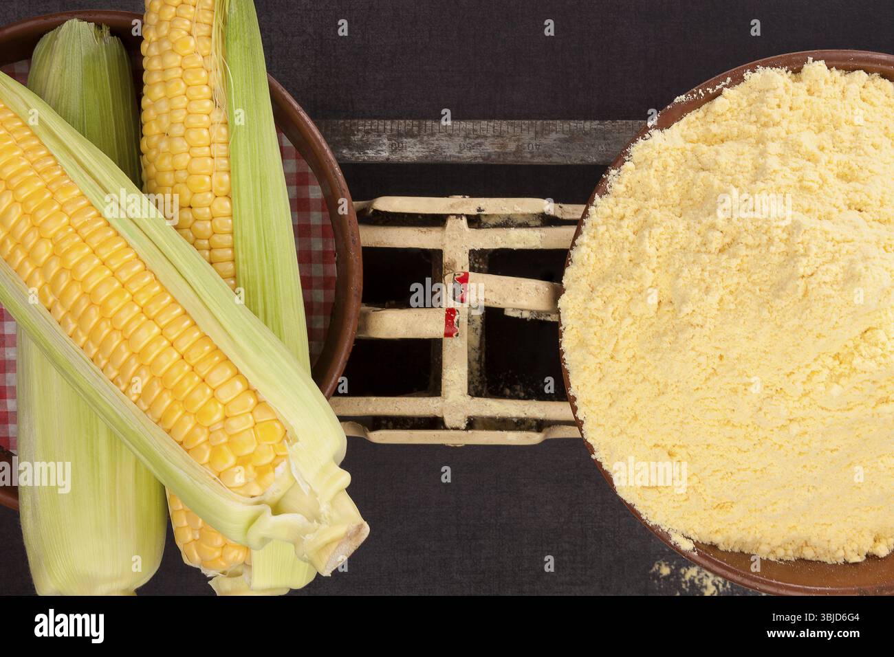 Corn cobs and corn flour on old weight scale from above. Dark surface ...