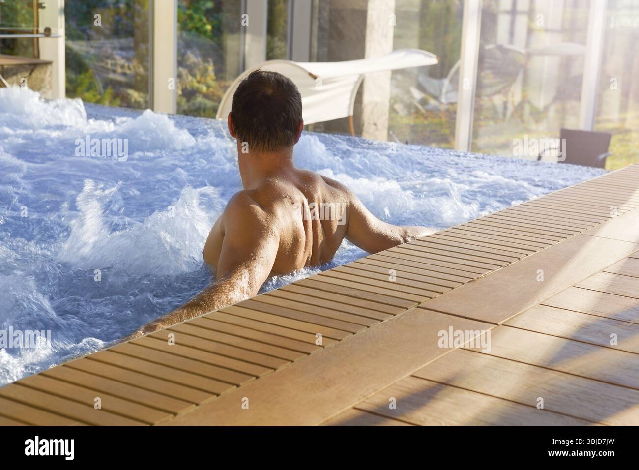 Handsome man in jacuzzi in luxurious hotel with big glass windows with ...