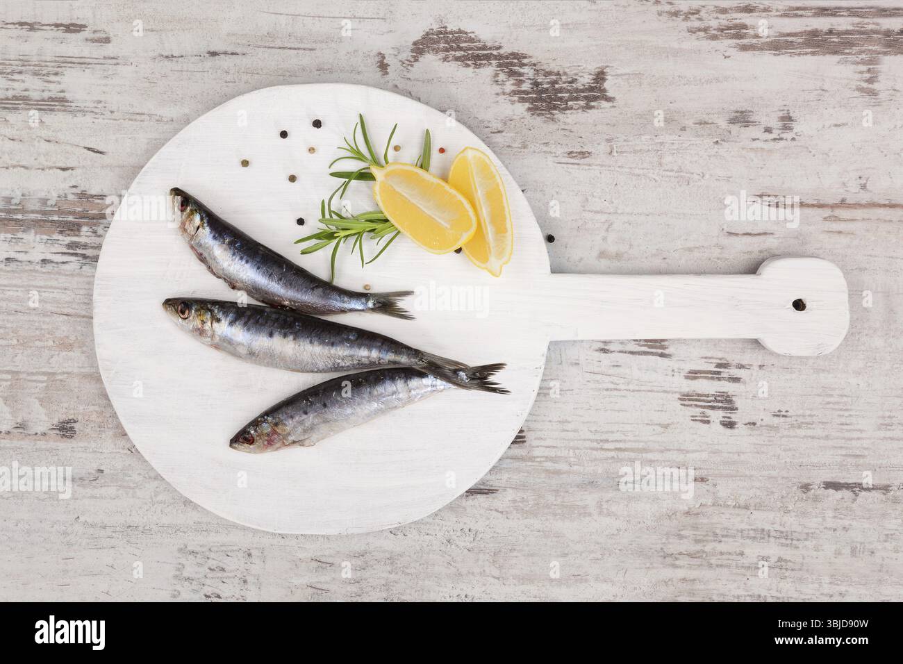 Three fresh anchovy fish on white round kitchen board on white wooden ...