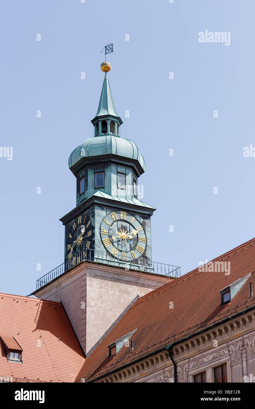 A clock tower with a verdigris roof stands against a pale blue sky ...