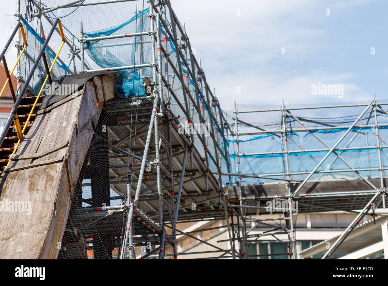 Construction scene with scaffolding, wooden ramp, blue safety netting ...