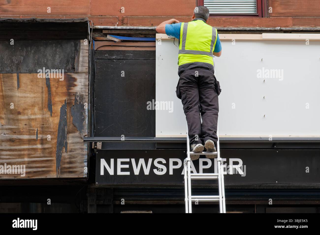 Tradesman installing new sign above shop using ladder Stock Photo - Alamy