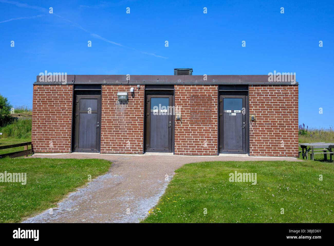 Three restroom stalls built from brick are situated near a walking path ...
