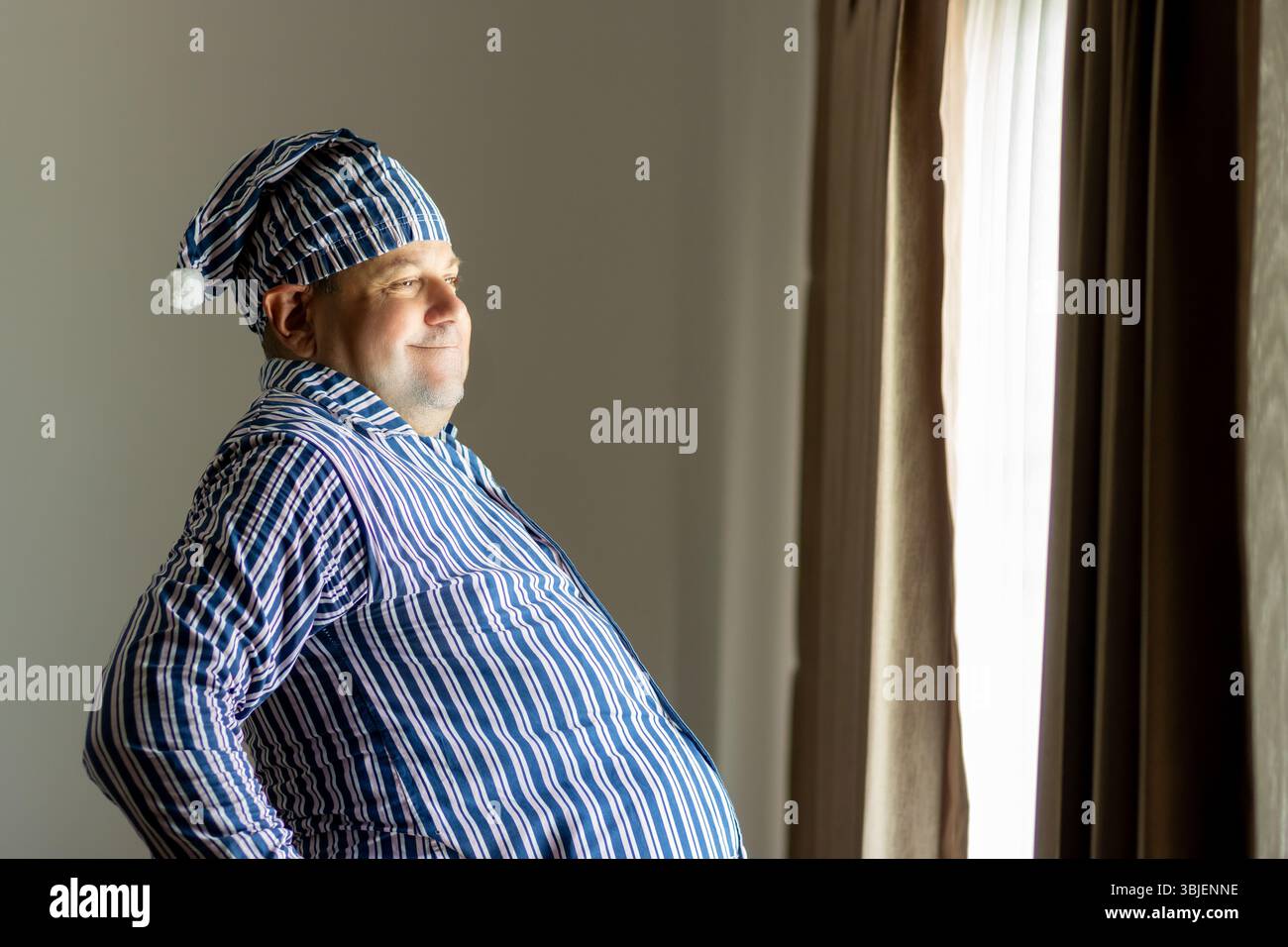 A fat man in striped pajamas looks out from a curtained window Stock ...