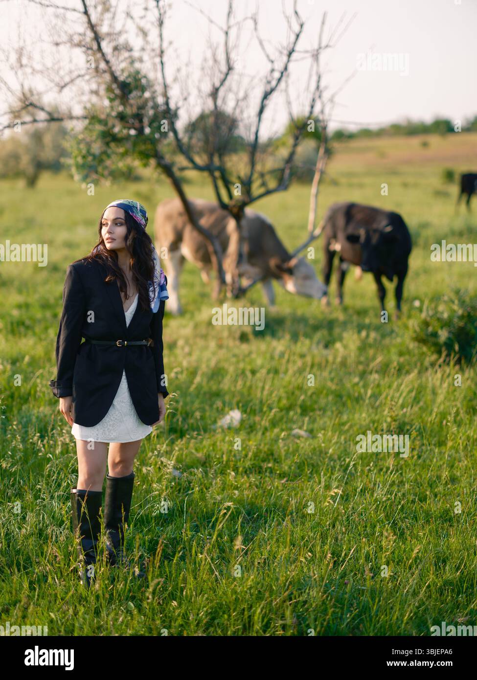 Young woman herding cows on a green pasture in the countryside. Rural ...