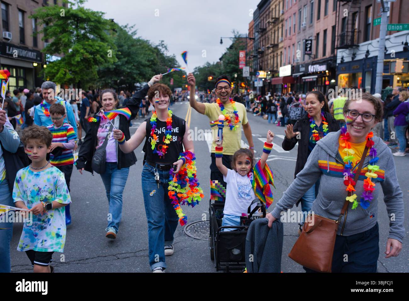 A diverse group of people, many wearing rainbow attire and leis, march ...