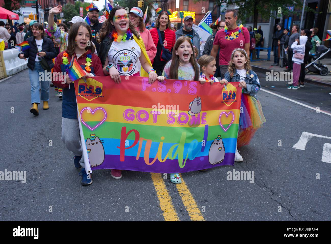 A group of children and adults at a Pride parade hold a large rainbow ...
