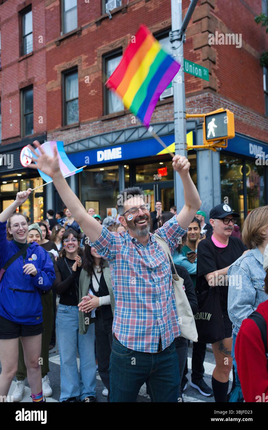 A jubilant man with glasses, wearing a plaid shirt and jeans, holds a ...