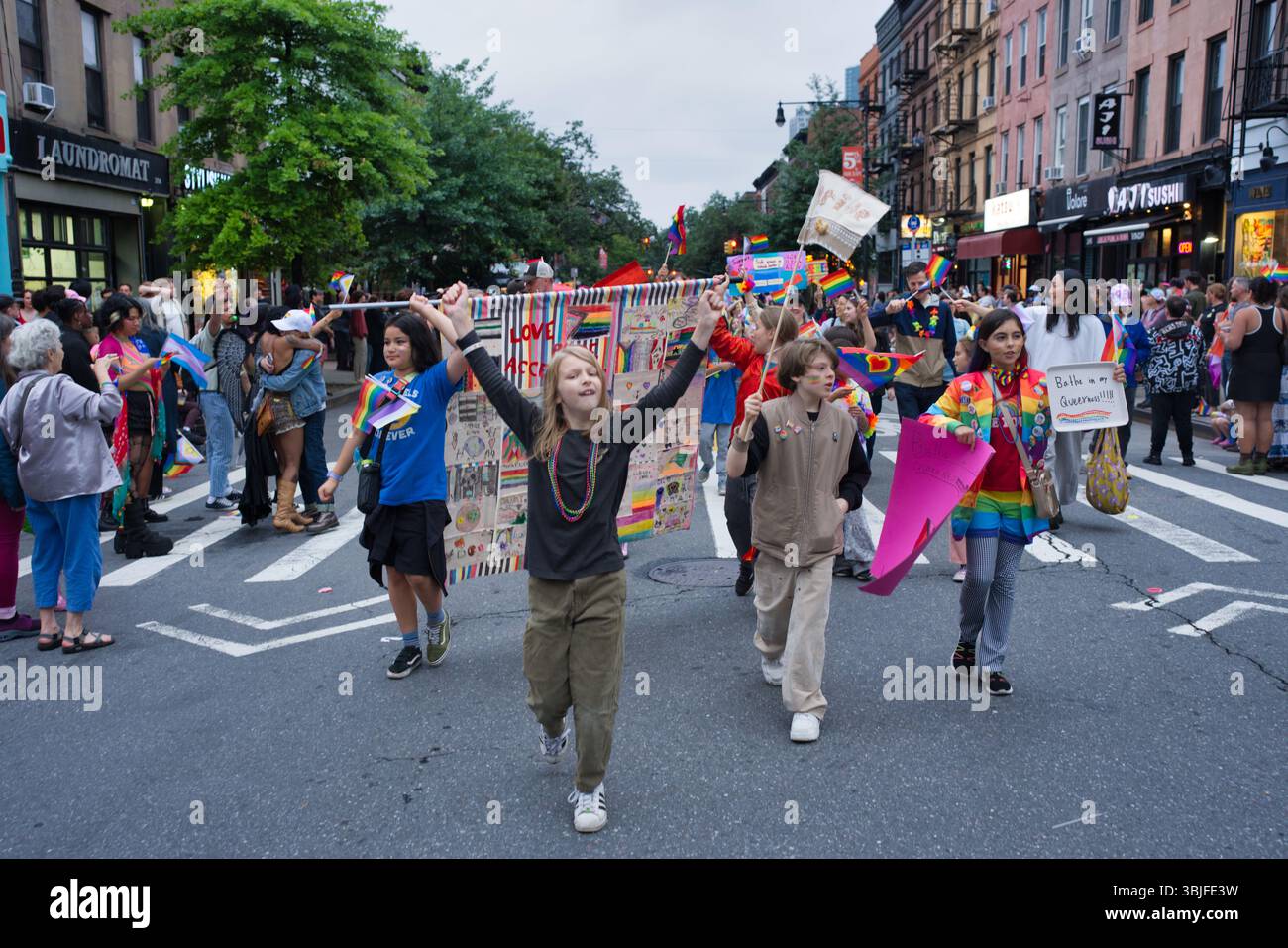 Children and adults participate in a Pride parade, carrying a large ...
