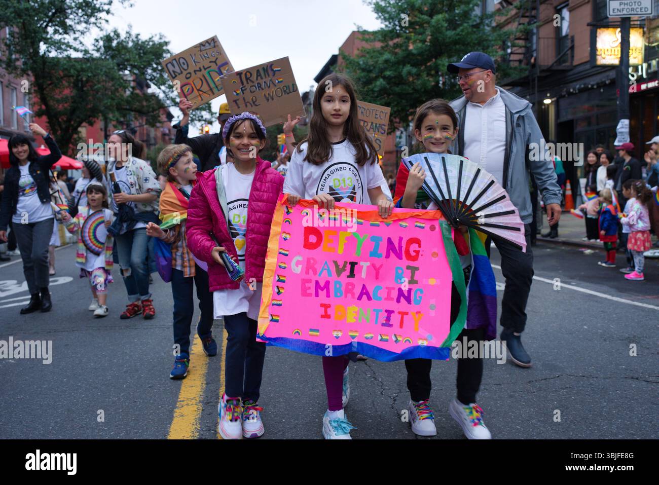 Children and adults participate in a Pride parade, carrying signs ...