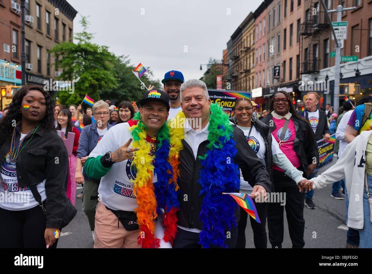 Two men, one wearing a rainbow boa, stand at a Pride parade amongst a ...