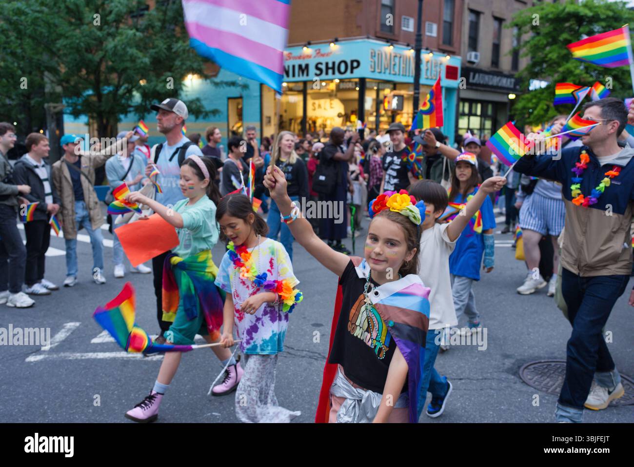 A vibrant street scene captures a Pride parade. Children and adults ...