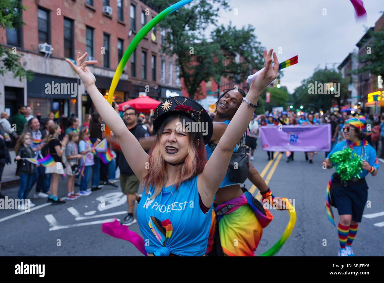 A vibrant Pride parade scene features a young woman with arms raised ...