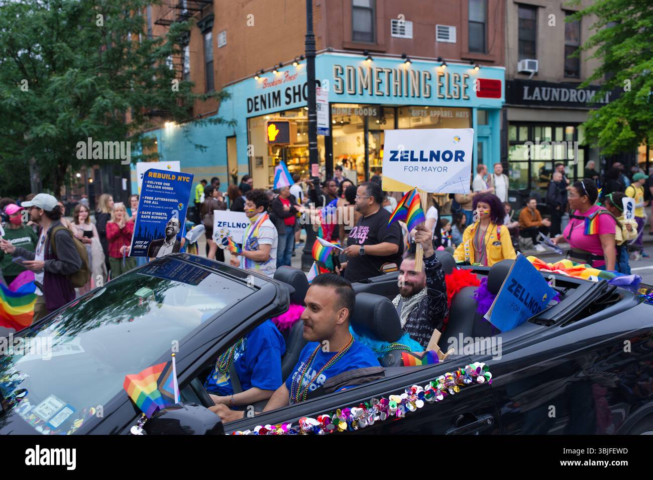 A black convertible car drives in a Pride parade, carrying people ...