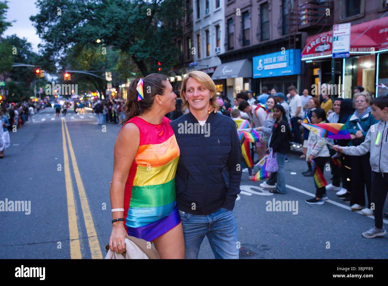 Two women, one in a rainbow dress, stand close together on a city ...