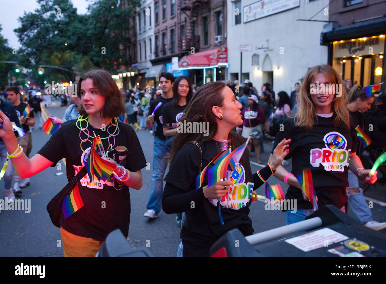 Three women participate in a nighttime Pride parade, holding rainbow ...