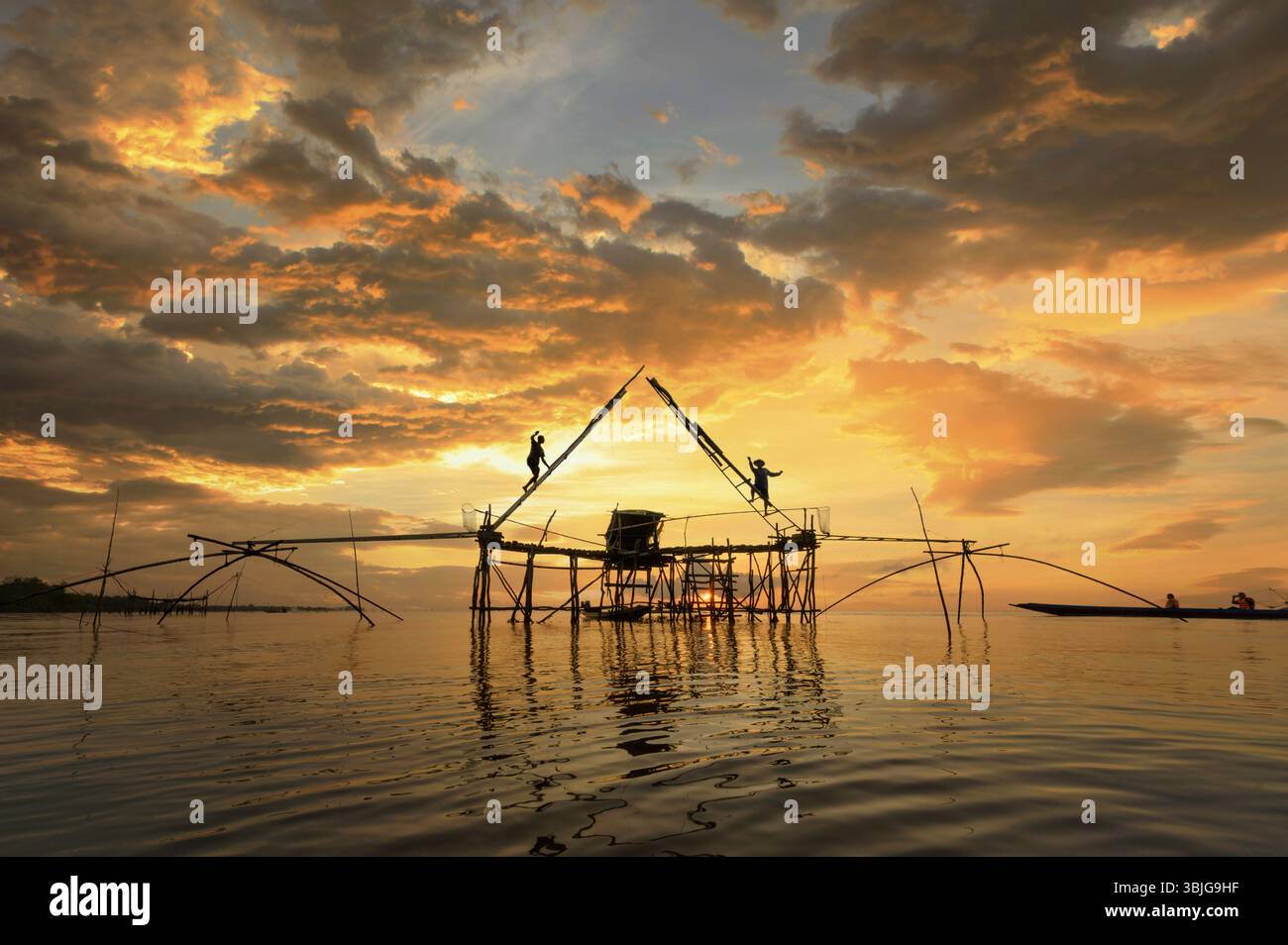 Silhouette of two men climbing on a traditional fishing trap at sunrise ...