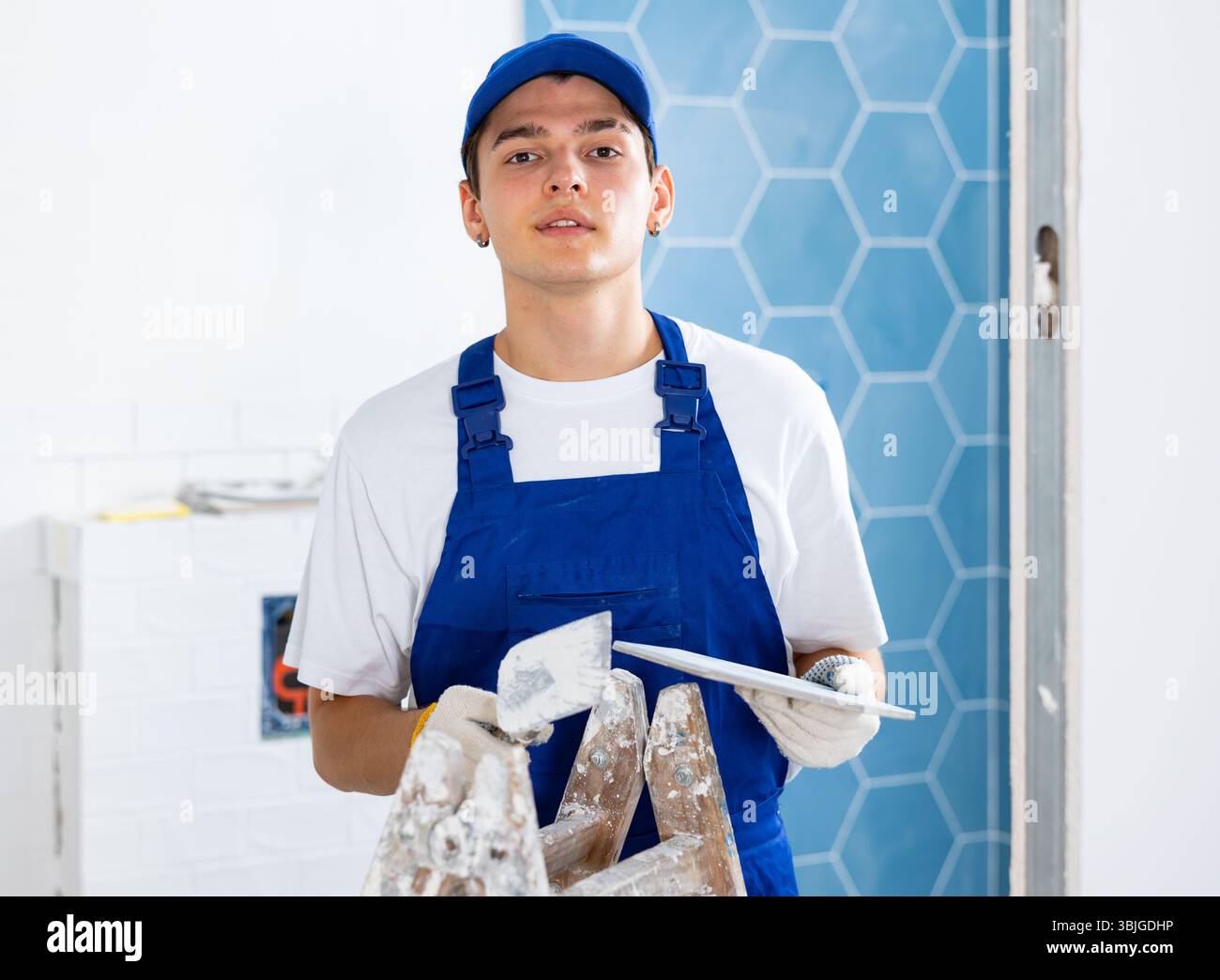 Construction worker in work clothes engaged in wall tiling work during overhauls indoors Stock ...